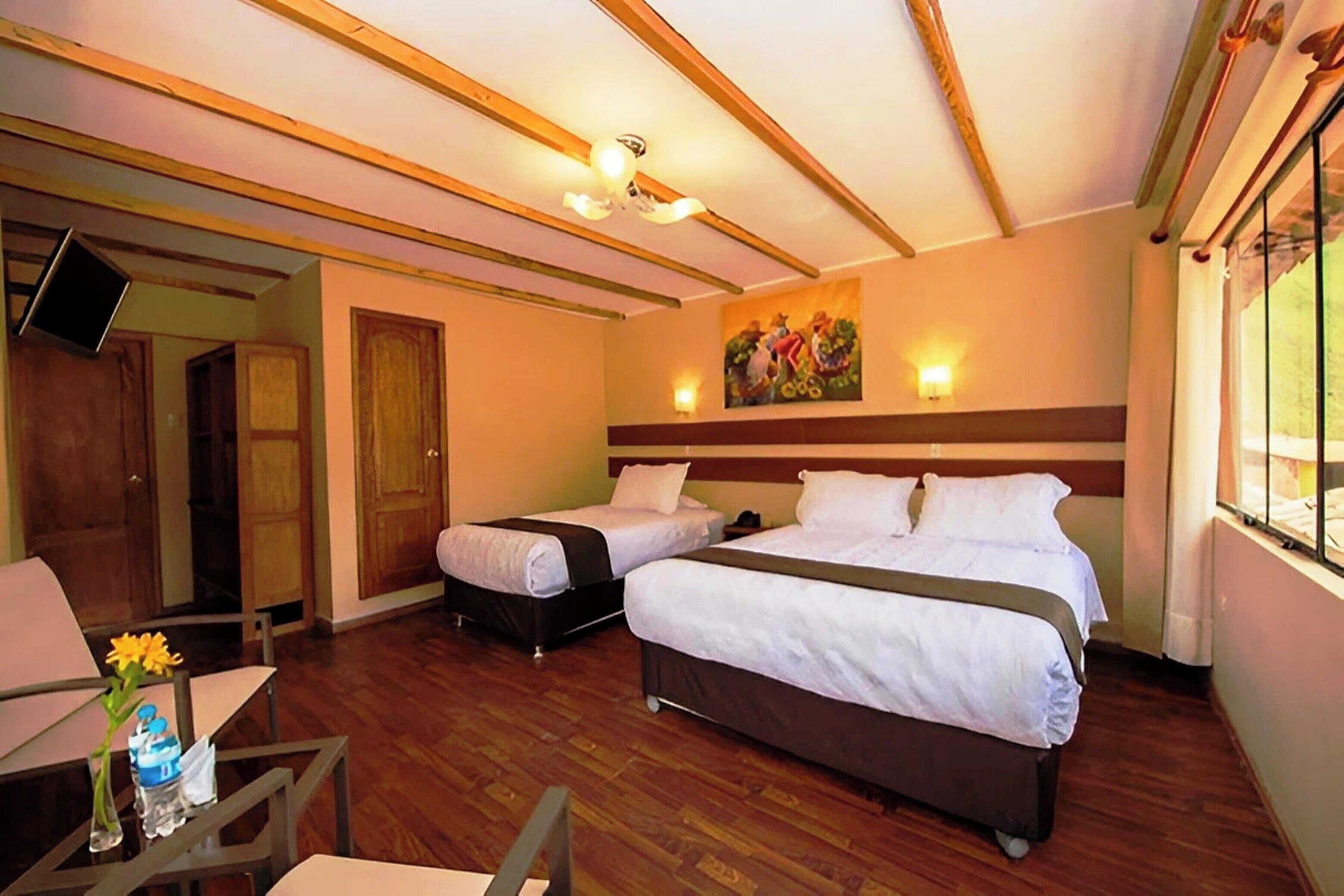 Quarto de hotel com duas camas de solteiro, uma escrivaninha com cadeira, uma televisão e um quadro na parede.