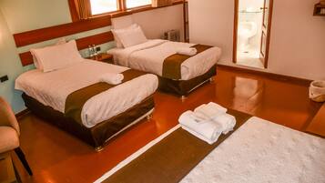 Quarto de hotel com duas camas, cada uma com cabeceira de madeira, uma mesinha com uma garrafa e uma cadeira.