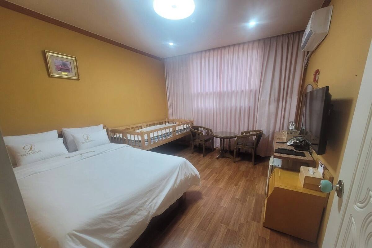 Quarto de hotel com cama, escrivaninha, cadeira, televisão e janela com cortinas.
