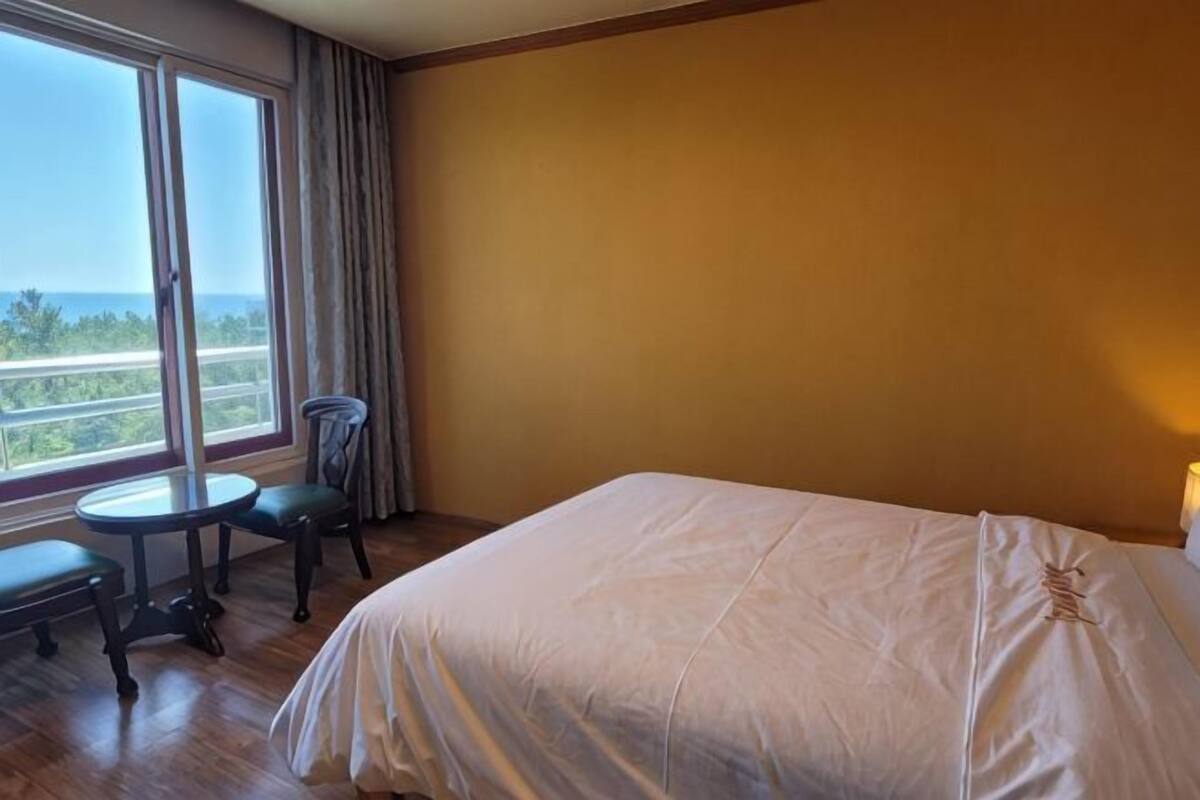 Quarto de hotel com uma cama grande, uma mesa pequena, uma cadeira e uma janela com vista.