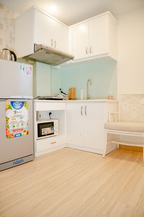 Cozinha compacta com armários brancos, micro-ondas embutido e exaustor de aço inoxidável.