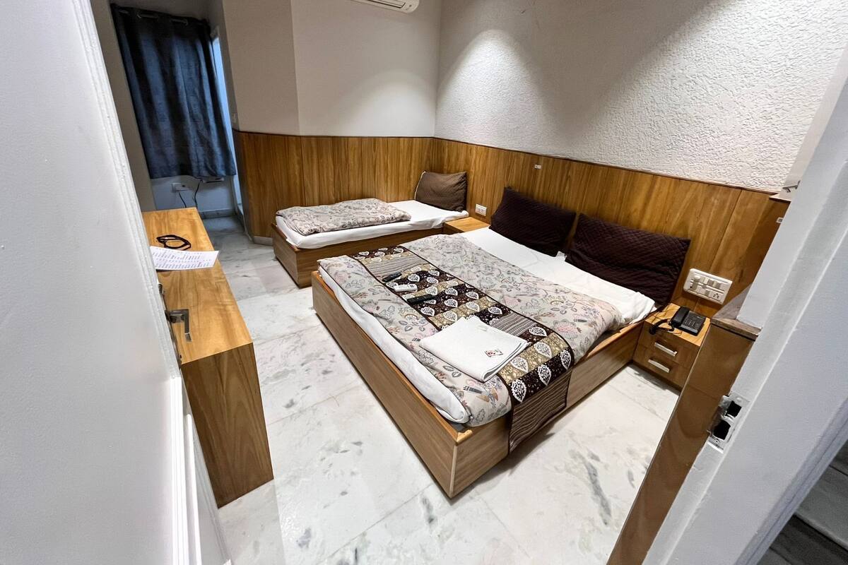 Quarto de hotel compacto com duas camas de solteiro, cabeceira de madeira, pequena escrivaninha com telefone e ar-condicionado fixado na parede.