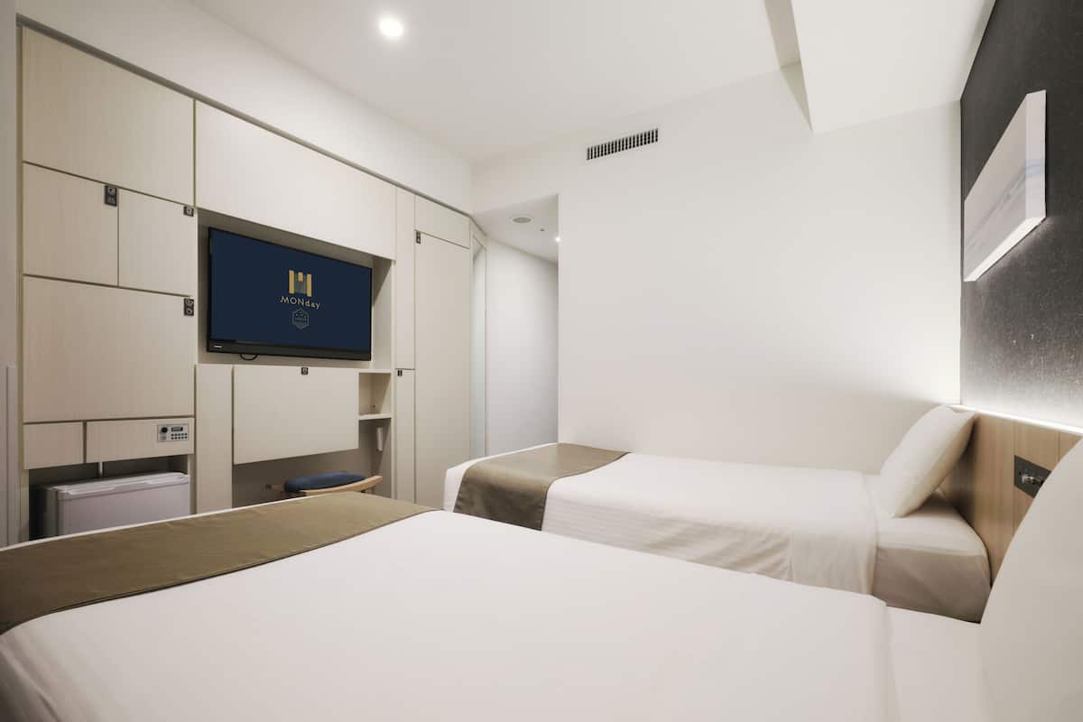 Quarto de hotel moderno com duas camas, televisão de tela plana e minibar.