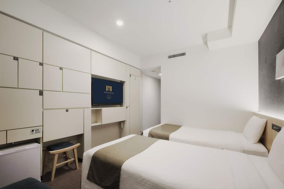 Quarto de hotel com duas camas, uma escrivaninha, televisão e guarda-roupa.