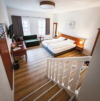 Quarto com cama, escrivaninha, cadeira, sofá, televisão e janela.