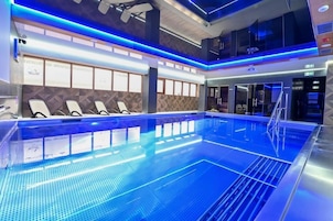 Piscina interior moderna com iluminação azul, cadeiras de descanso e um mezanino.