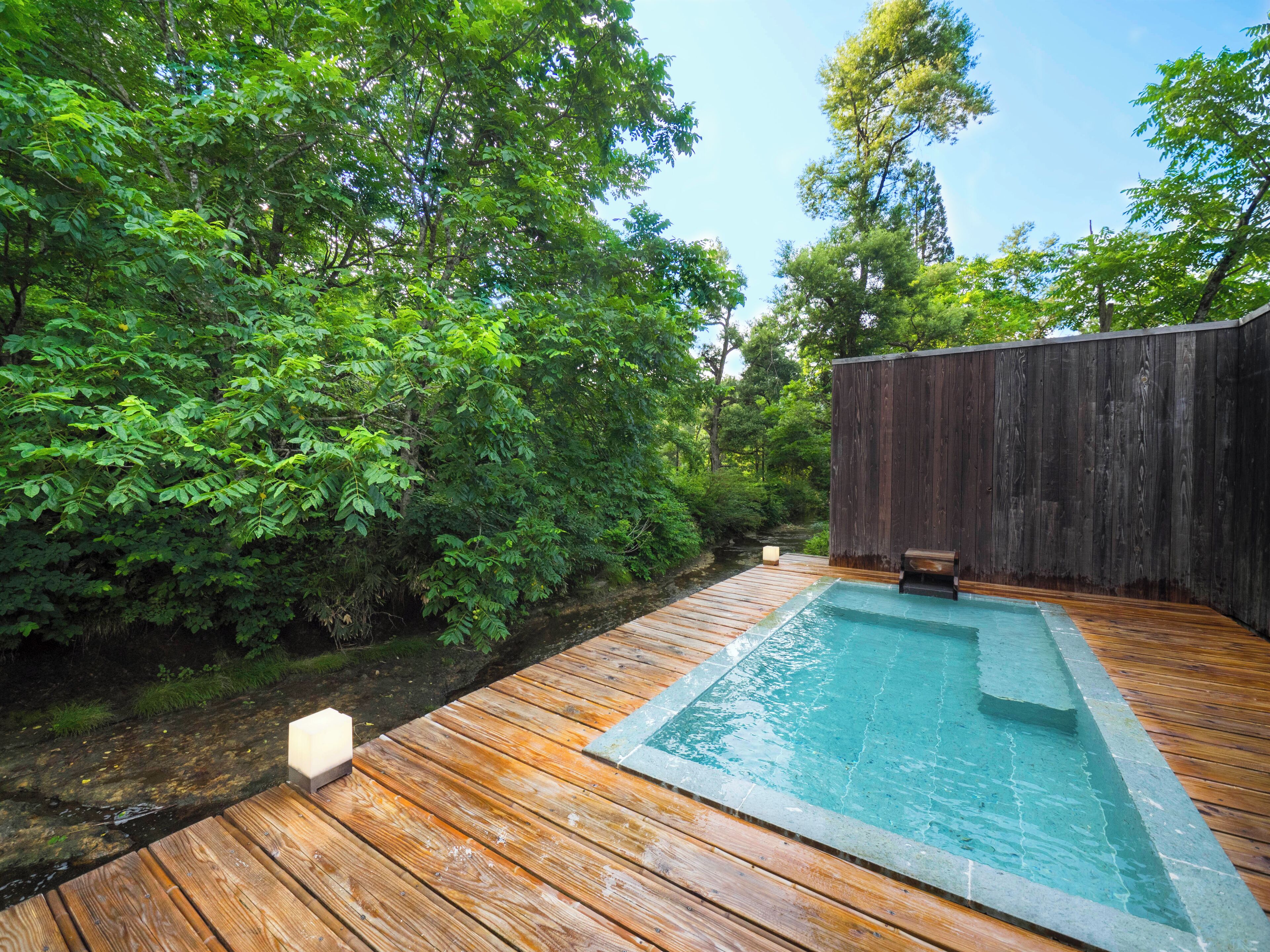 Um deck de madeira com uma piscina retangular, cercado por folhagem verde exuberante e um cercado de madeira.