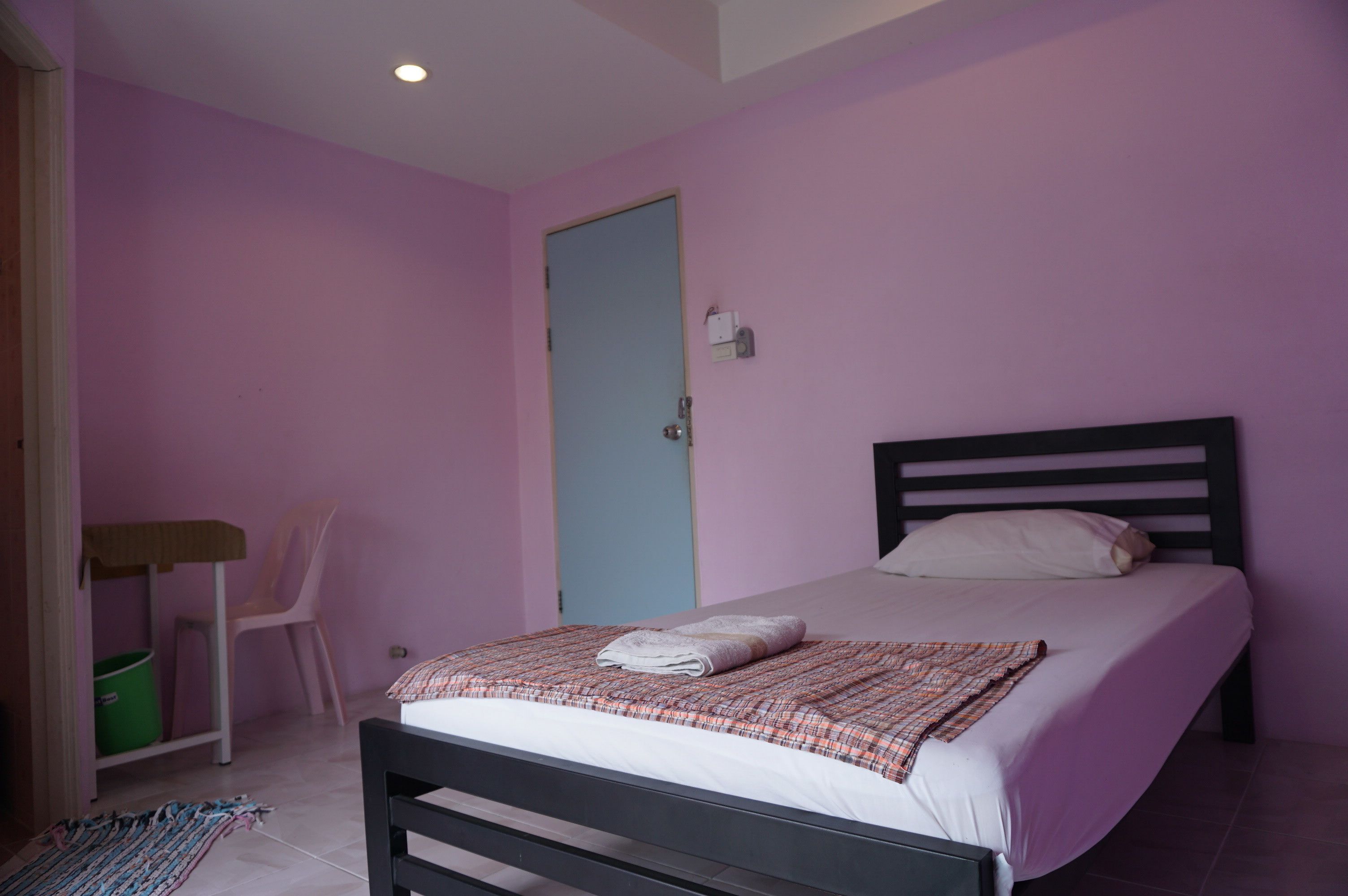 Um quarto com uma cama, uma cadeira, uma mesinha e uma porta.