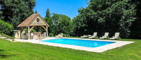 Piscina com espreguiçadeiras e um gazebo em um quintal gramado.