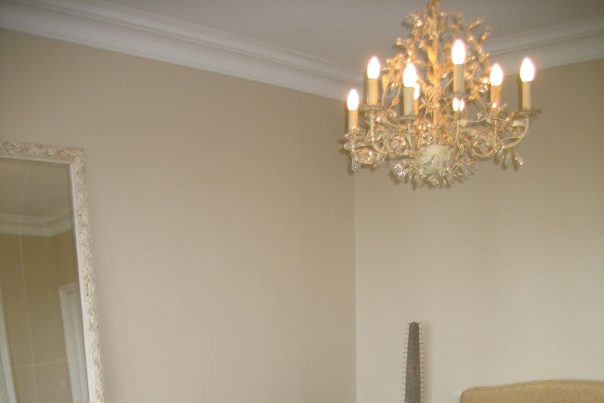 Quarto com uma cama grande, um banquinho, cômoda, espelho e um lustre.
