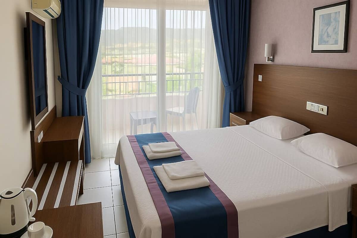 Quarto de hotel com uma cama, uma escrivaninha com luminária, uma cadeira e vista para o exterior.