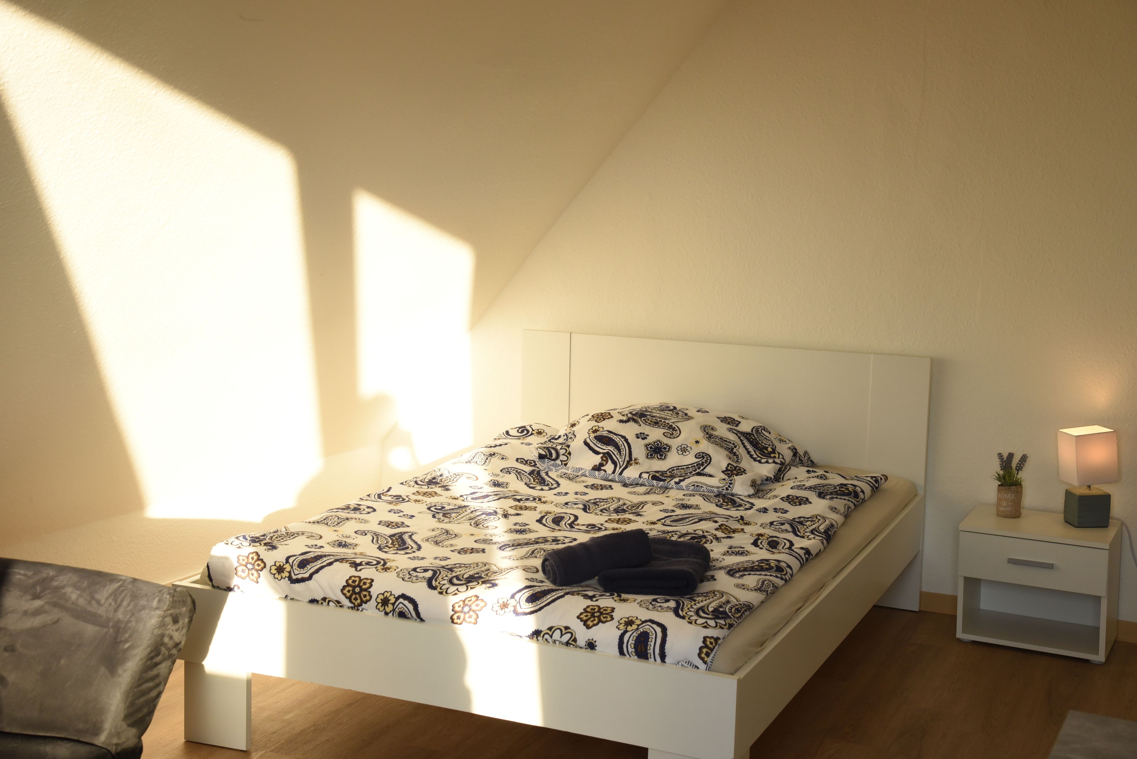 Quarto com cama, mesa de cabeceira e abajur.