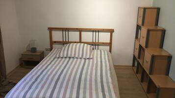 Quarto com estrutura de cama de madeira, mesa de cabeceira com abajur e armário embutido de madeira.