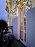 Fachada de um edifício com varanda, mesa e cadeiras, e uma porta.