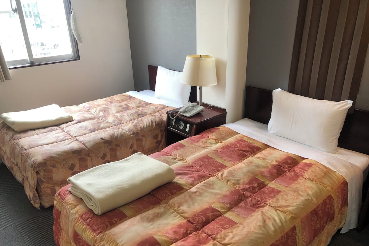 Quarto de hotel com duas camas, cada uma com colcha estampada, luminária de cabeceira e telefone em uma mesinha de cabeceira.