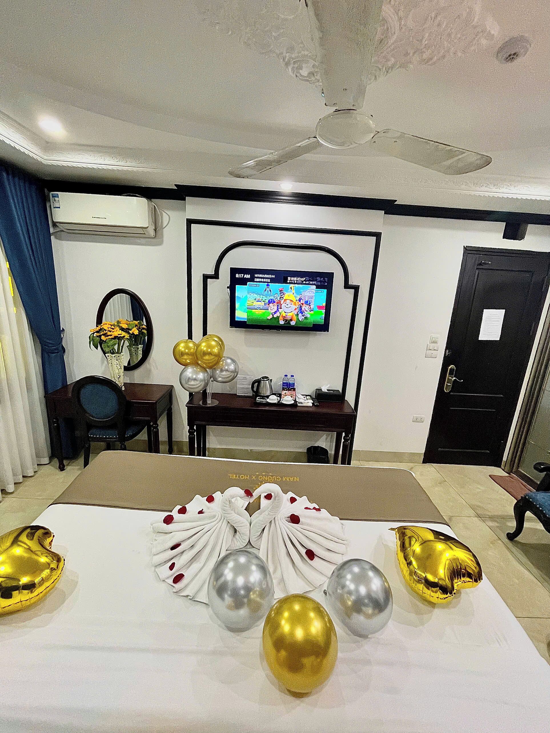 Quarto de hotel com cama, televisão na parede, secretária com cadeira e porta.