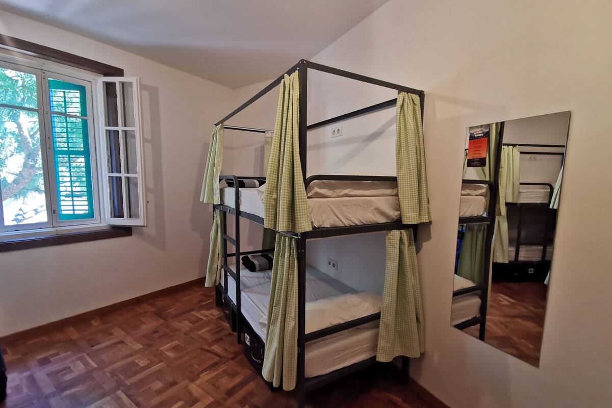 Quarto com beliche, janela, soalho de madeira e espelho na parede.