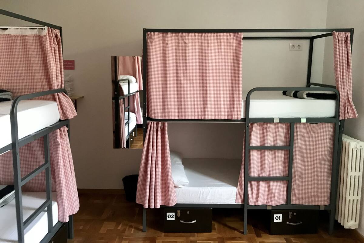 Quarto de dormitório com beliches, cada um com colchão e travesseiro, e uma gavetinha de armazenamento embaixo de uma cama.