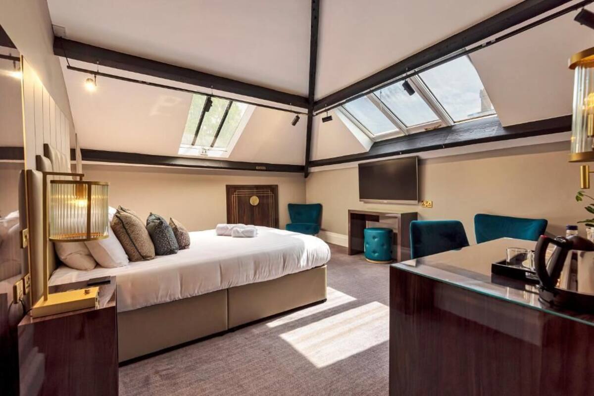 Quarto de hotel moderno com uma cama grande, uma mesa de escritório e uma televisão. Há claraboias e vista para a cidade.