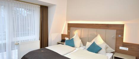 Quarto de hotel com uma cama grande, cabeceira de madeira e mesa de cabeceira com abajur.