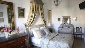 Quarto com cama de dossel, cômoda, penteadeira com espelho e lustre.