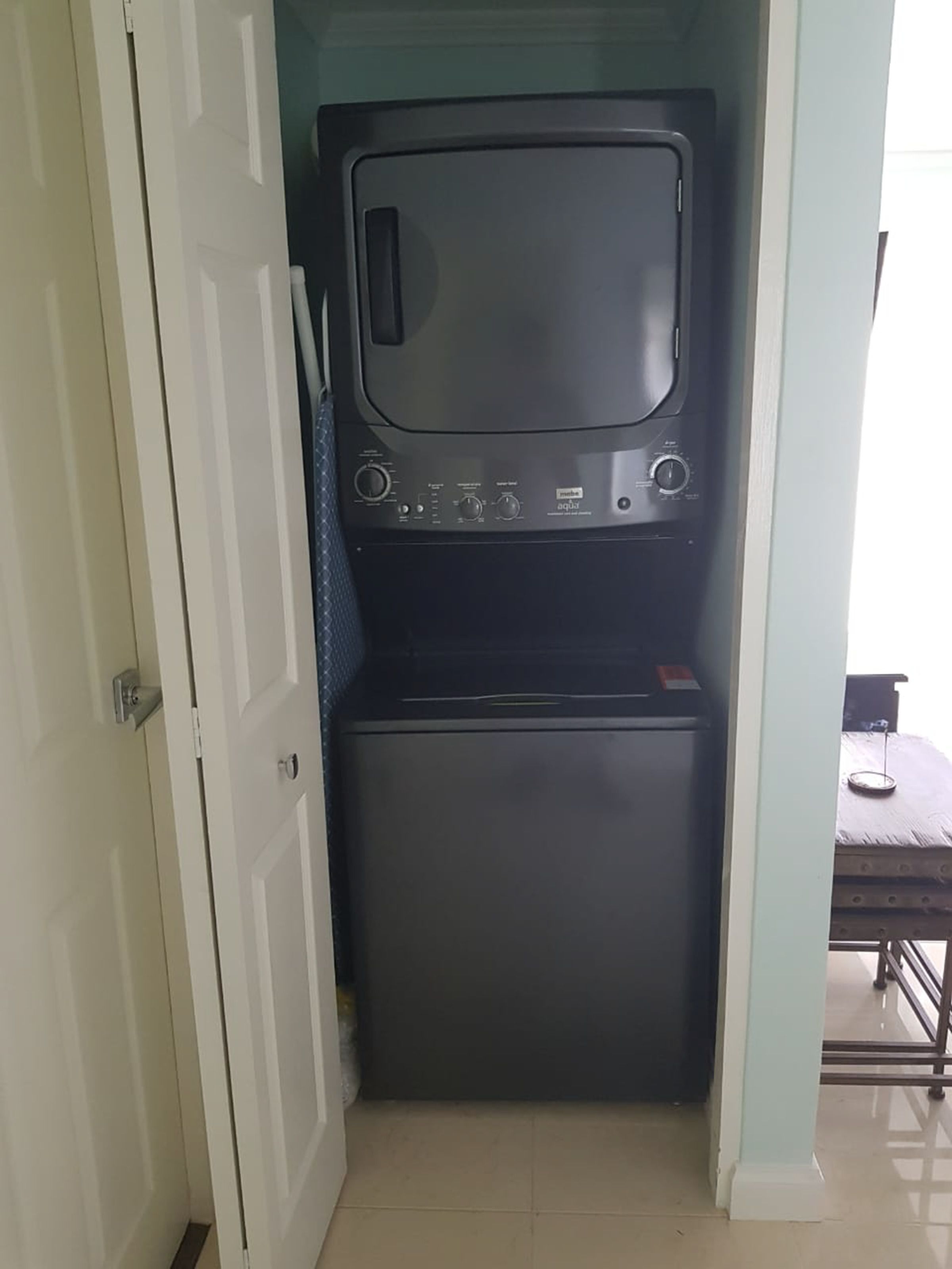 Uma lavanderia compacta com máquina de lavar e secadora, uma porta e chão revestido com azulejos.