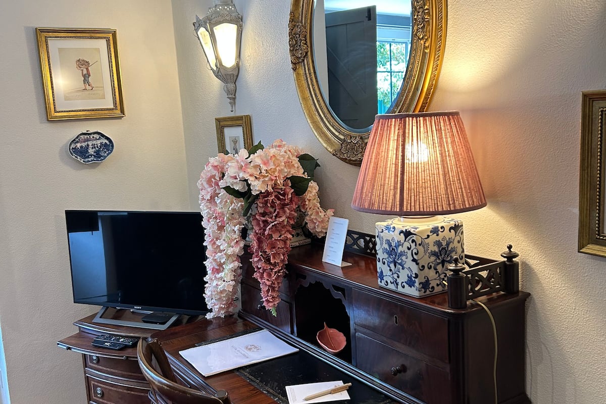 Quarto bem mobiliado com escrivaninha de madeira, televisão, luminária e um espelho grande.