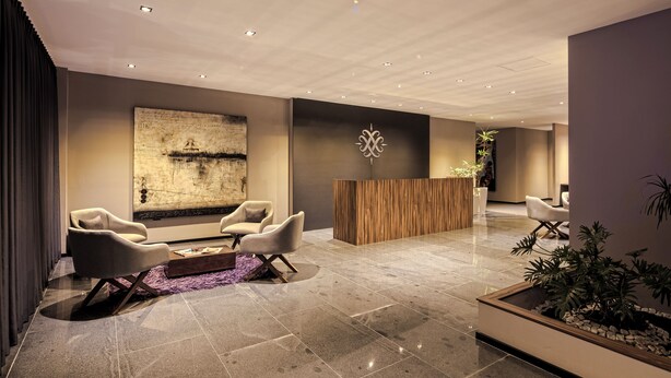 Um lobby moderno com balcão de recepção, duas áreas de estar e uma grande pintura abstrata na parede.