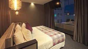 Quarto de hotel moderno com uma cama grande, televisão de tela plana e vista para a cidade à noite.