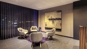 Um interior moderno com três cadeiras, uma grande pintura abstrata e vista da cidade através de cortinas translúcidas.