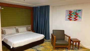 Quarto de hotel com cama, cadeira, mesa pequena e um quadro na parede.
