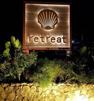Uma placa de madeira com design de concha e a palavra 'retreat' iluminada à noite.