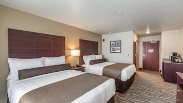 Quarto de hotel com duas camas, uma mesa de trabalho, uma luminária e uma porta para o banheiro.
