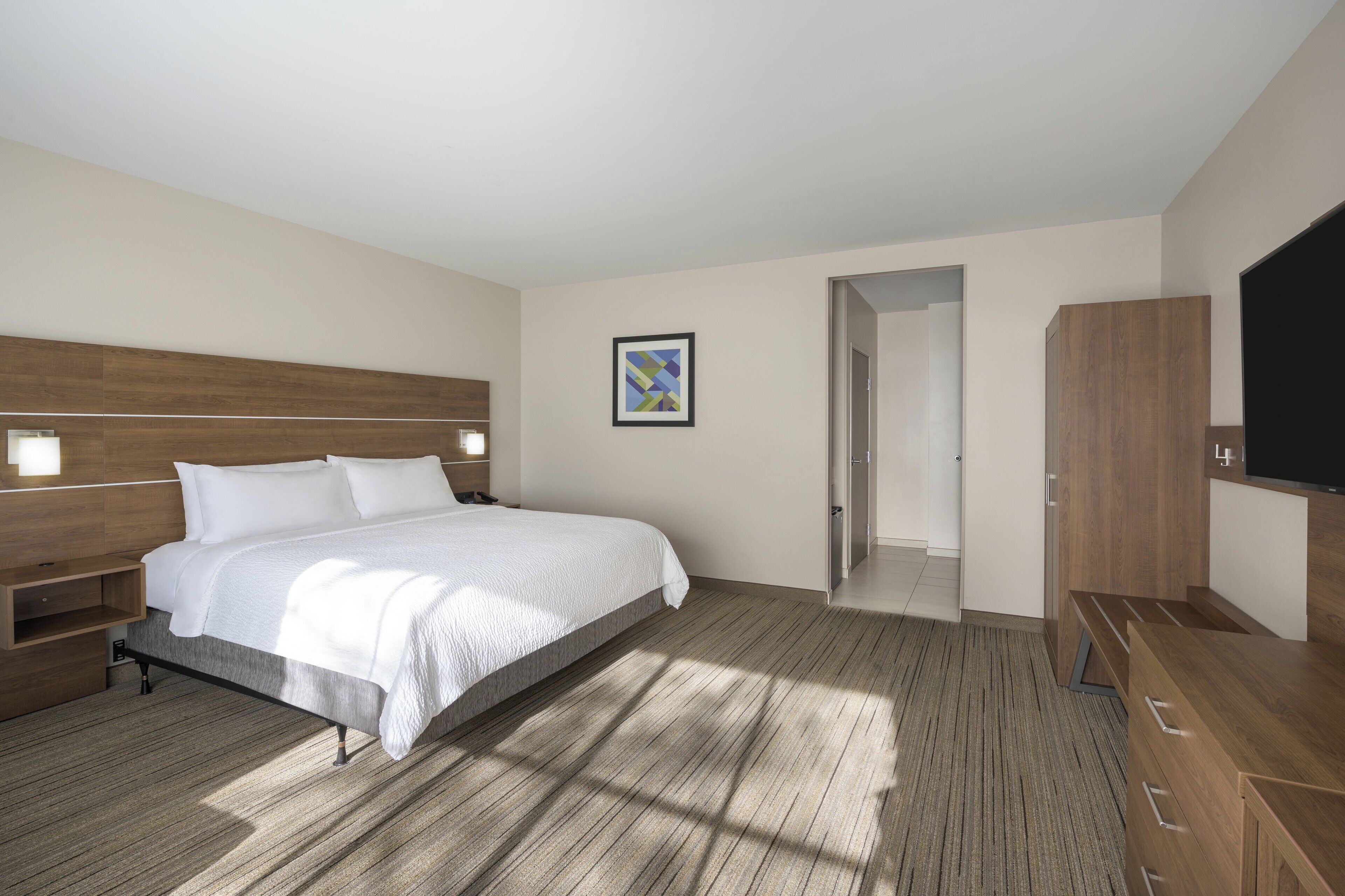 Quarto de hotel moderno com uma cama grande, cabeceira de madeira, televisão de tela plana e guarda-roupa.