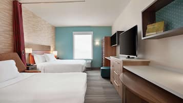 Quarto de hotel com duas camas, uma escrivaninha, uma televisão e uma janela.