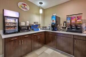 Espaço de café da manhã com geladeira, torradeira, cafeteira e dispensadores de iogurte.