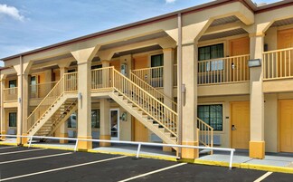 Um motel de vários andares com escadaria central, varandas e estacionamento.