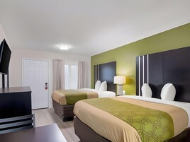 Quarto de hotel com duas camas, uma televisão, uma escrivaninha e uma porta.