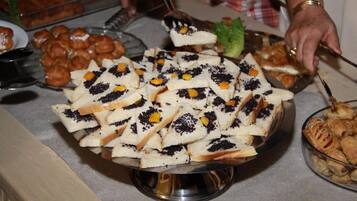 Um buffet com diversos alimentos, incluindo pão com sementes de papoula e pedaços de laranja, e uma pessoa servindo.
