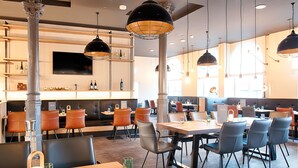 Interior moderno de restaurante com pé direito alto, iluminação pendente e diversas opções de assentos.