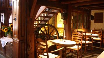 Um interior rústico com móveis de madeira, uma grande roda de madeira e uma pequena mesa com cadeiras.