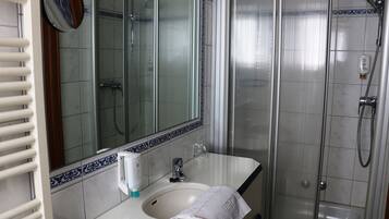 Uma casa de banho com uma pia branca, um espelho, uma toalha e cabine de duche.