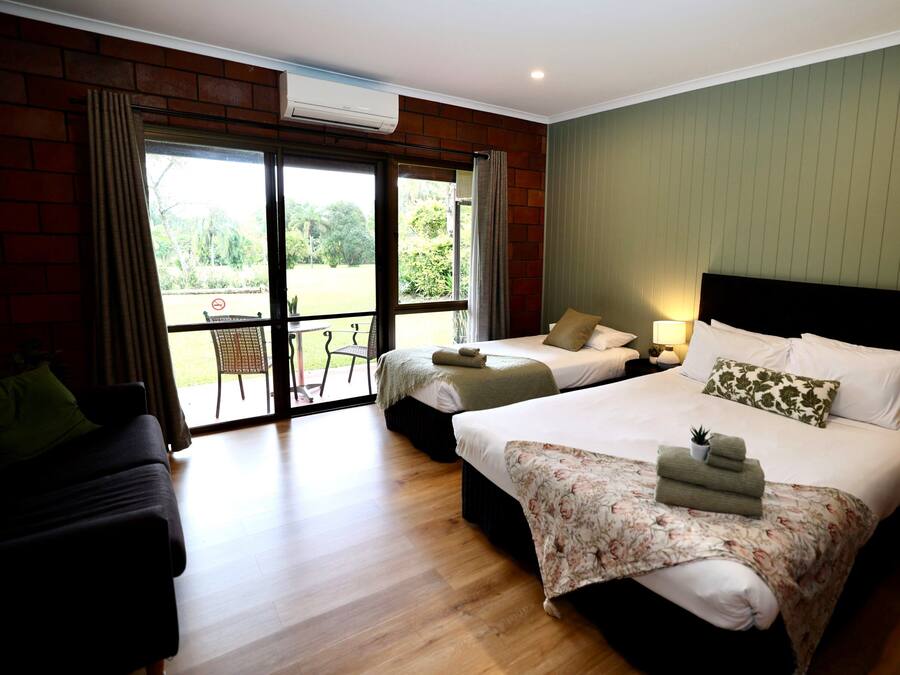 Quarto de hotel com duas camas, um sofá e uma porta de vidro que se abre para uma área externa.