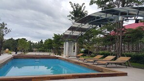 Piscina com deck de madeira, espreguiçadeiras e área coberta com telhado metálico.