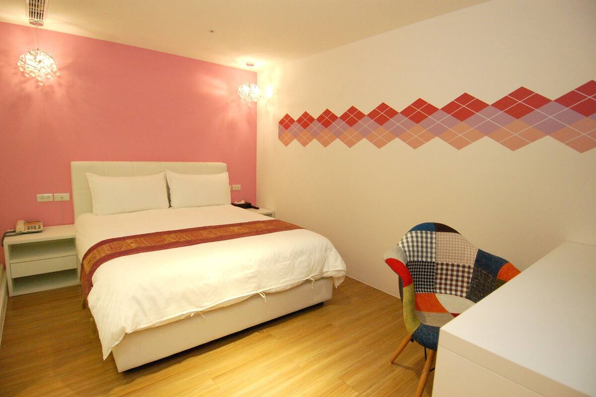 Quarto com cama, mesa de cabeceira, cadeira e parede com padrão geométrico.