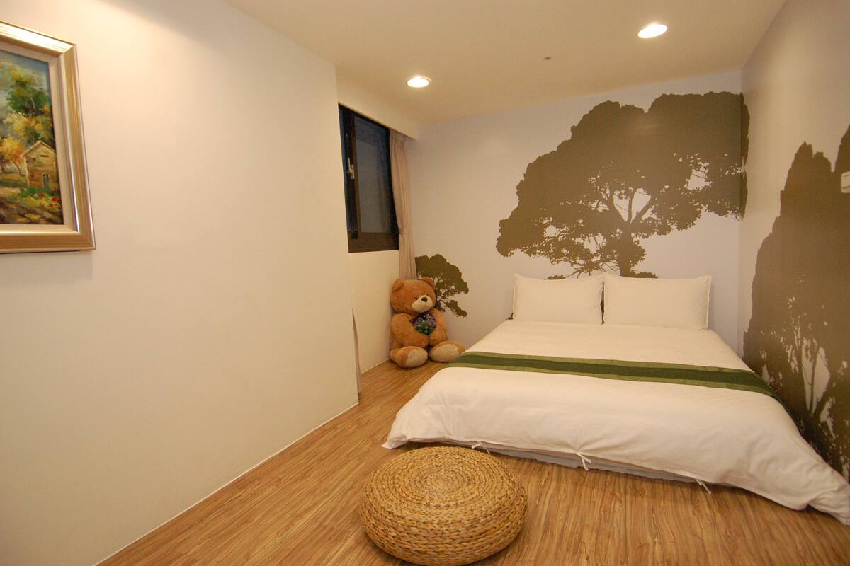 Quarto com cama, um urso de pelúcia, um quadro e um mural de uma árvore.