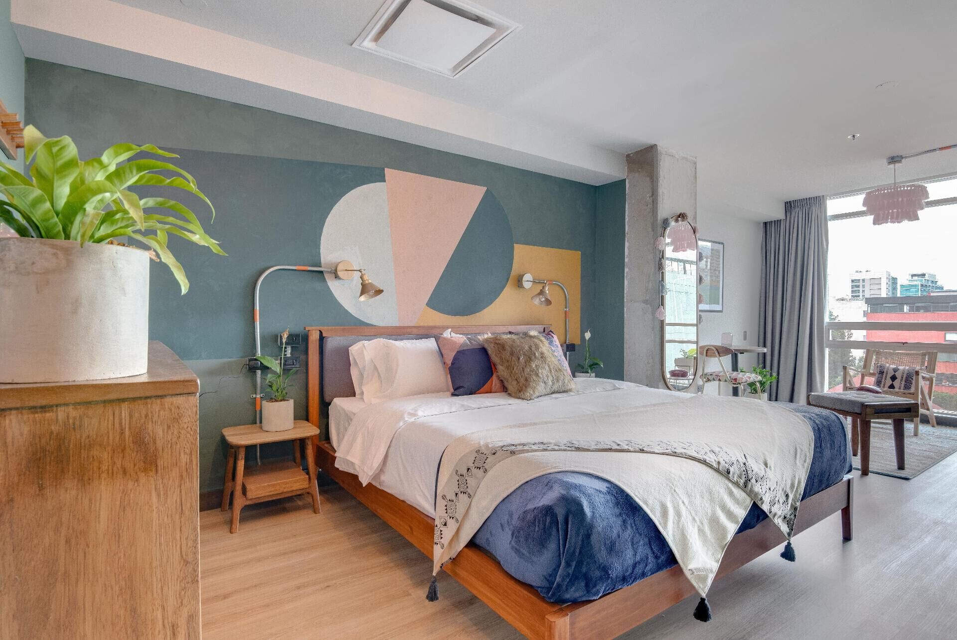 Quarto moderno com uma cama grande, um vaso de planta, uma escrivaninha e vista para a cidade.