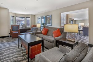 Quarto de hotel com sofá, poltronas, mesa de centro e área de refeições com mesa e cadeiras.