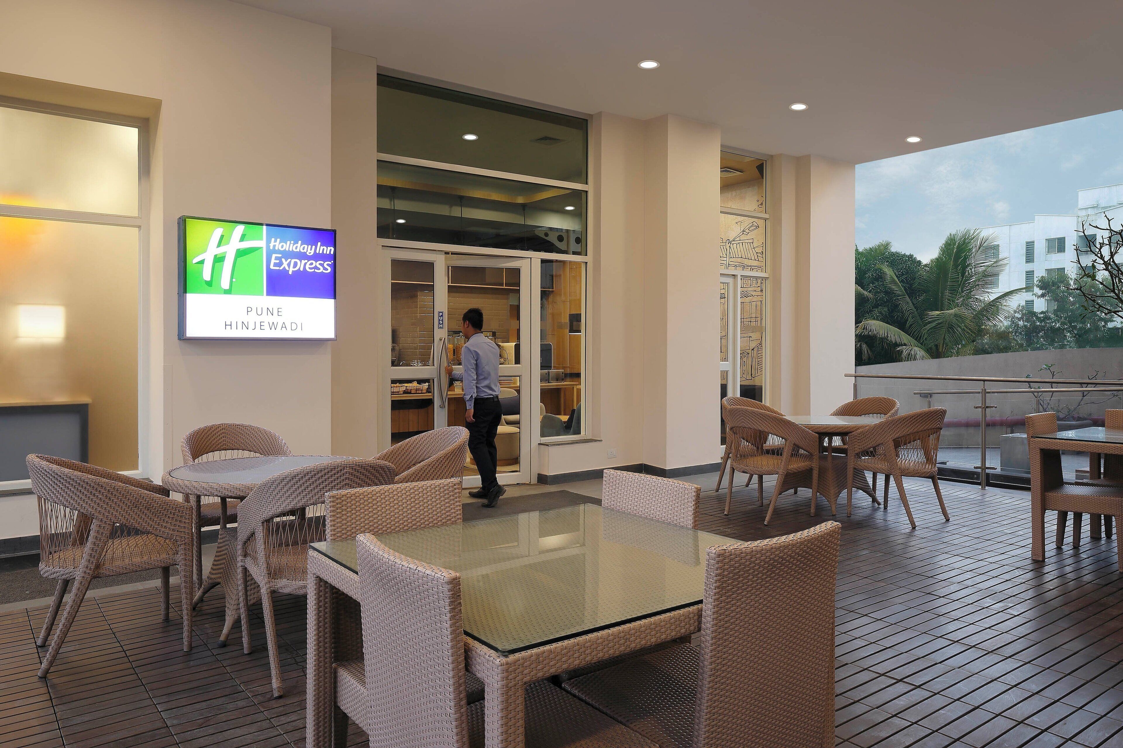 Uma área de estar externa com móveis de vime e uma mesa de vidro, um letreiro Holiday Inn Express e vista para a paisagem urbana.
