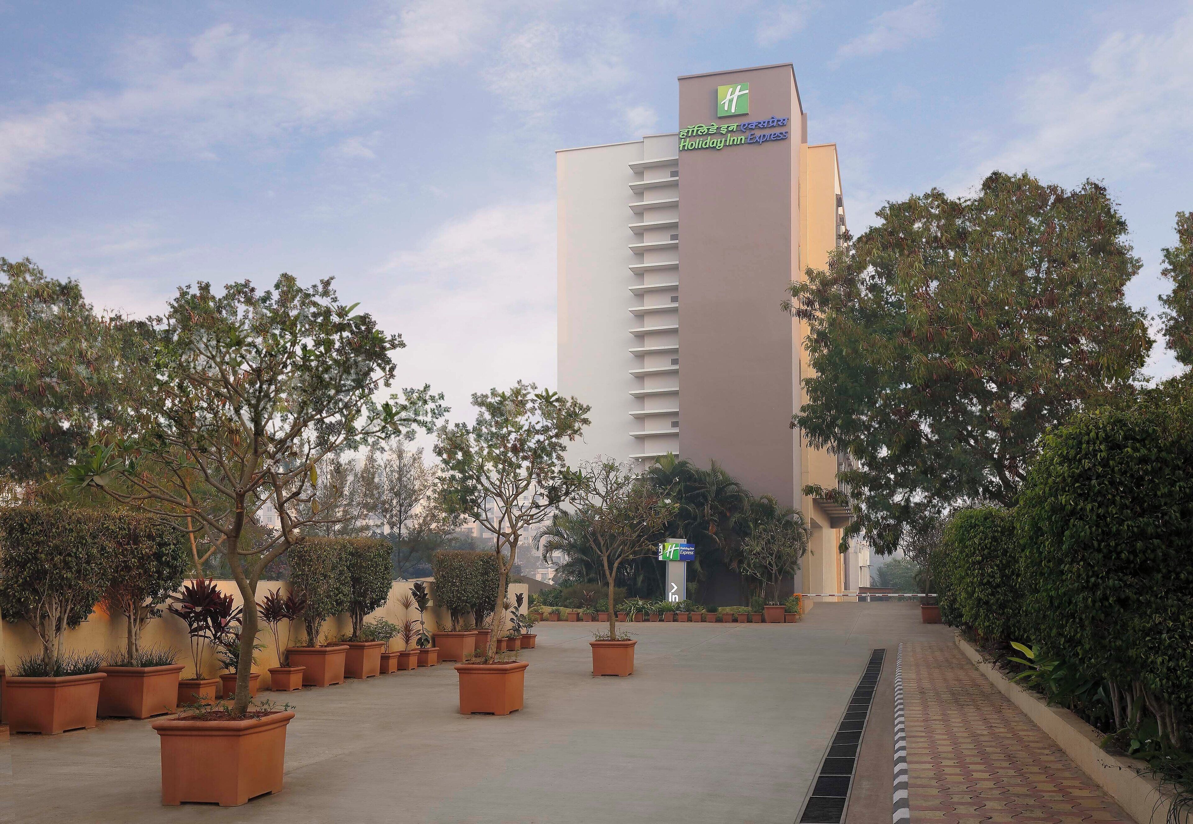Edifício Holiday Inn Express com céu claro, cercado por plantas em vasos e um calçadão pavimentado.